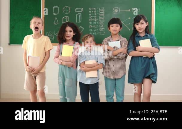 Multicultural elementary student in casual cloth looking at camera while standing at classroom ...