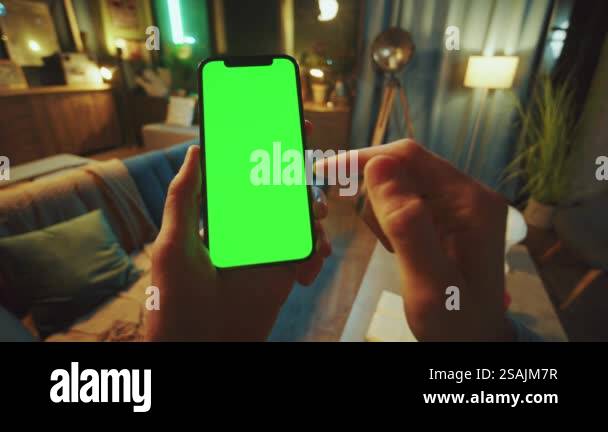 Close up man holds a scrolling phone with a vertical green screen in a ...