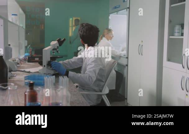 Young team of happy scientists with glasses looking under a microscope ...