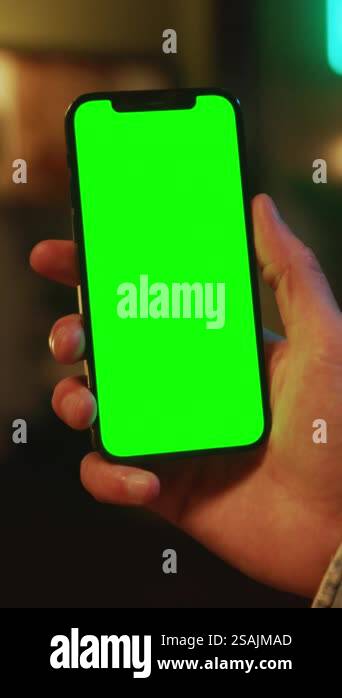 Hands man holding and using mobile phone with a vertical green screen indoors. Social media ...
