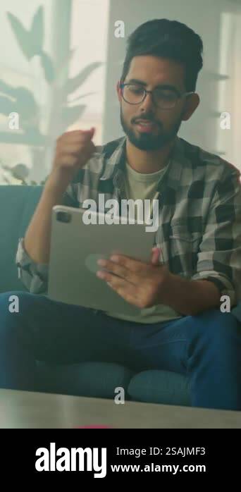 Handsome bearded man with glasses use tablet computer sitting on sofa ...
