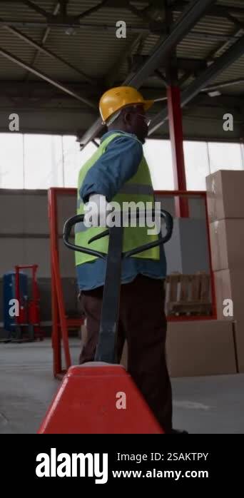 Full vertical follow shot of black male porter in overalls, denim shirt ...