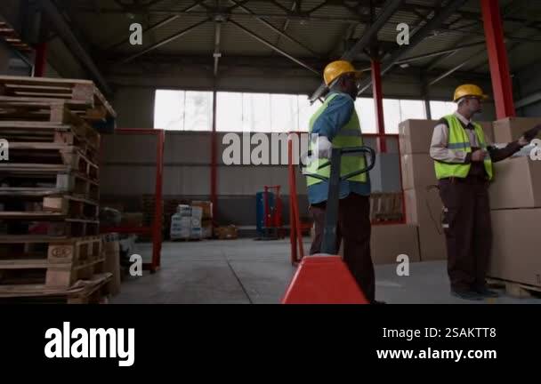Medium follow shot of African American male warehouse porter in safety ...