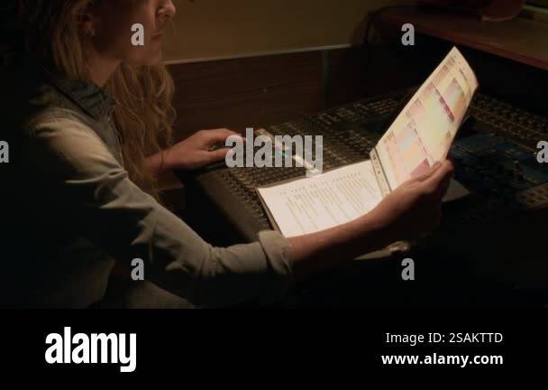 Medium closeup of young female TV producer sitting in small booth ...
