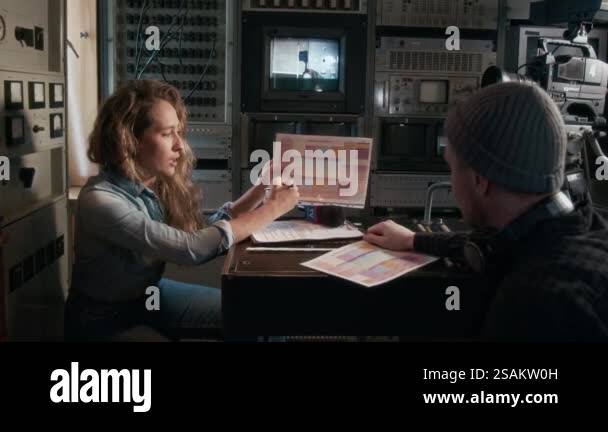 Medium shot of young female journalist and cameraman sitting together ...