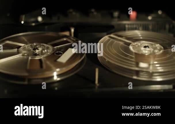 A close-up shot shows two reels of an old tape player spinning ...
