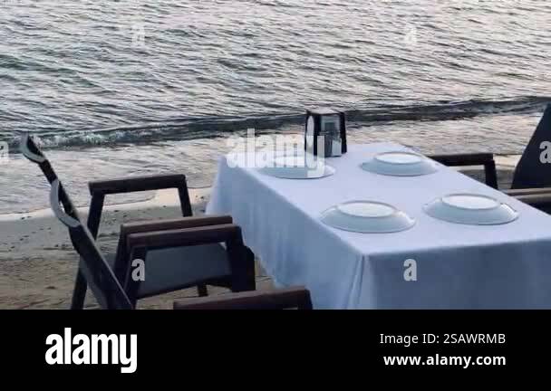Seaside dining table set for four overlooks gentle waves, offering a perfect setting for a ...
