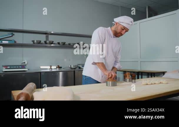 Professional chef in a white uniform using a dough cutter to create ...