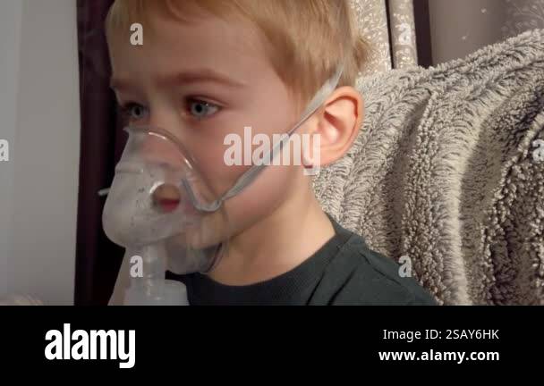 A young child sits comfortably while using a nebulizer to help with ...