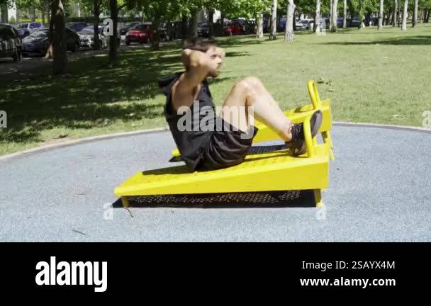 Young man doing sit-ups on an outdoor fitness park sit-up bench with ...