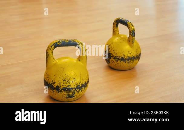 Two used and ruined yellow kettlebells.Time-worn gym tools on a wooden ...
