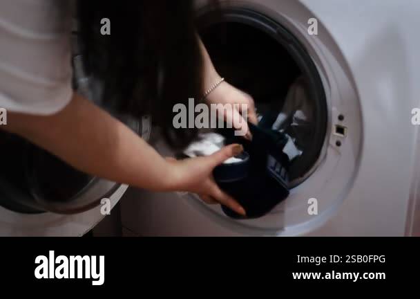 Young woman unloading laundry from a washing machine in a bright and ...