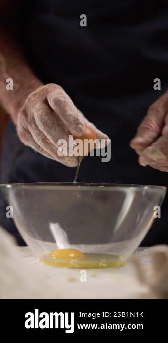 Close-up of baker s hands cracking an egg into a transparent bowl ...