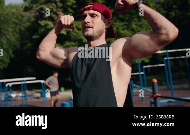 A muscular man is flexing his biceps on an outdoor sports field. He ...