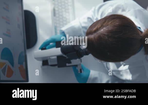 In a lab, a focused scientist examines samples under a microscope ...