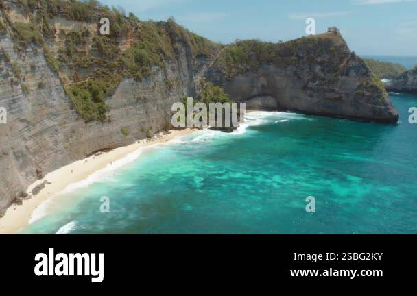 Secluded beach beneath towering cliffs, with turquoise waves crashing ...