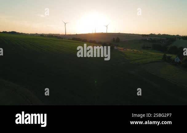 Sunset bathes rolling green fields and wind turbines in soft orange ...