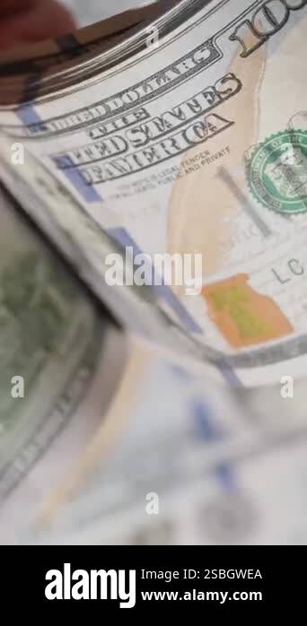 Vertical video. Holding and fanning out a stack of crisp hundred-dollar ...
