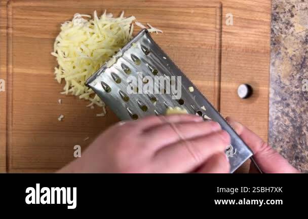 Grating hard cheese on a large metal grater against a wooden board. Top ...