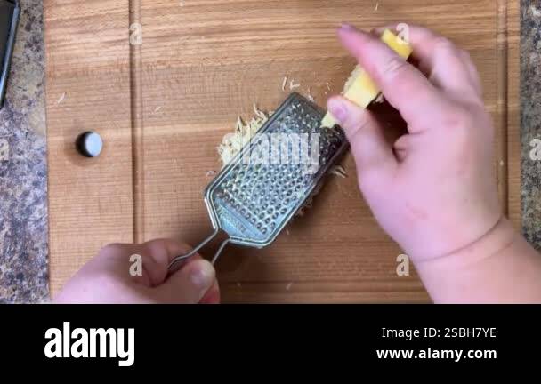 Grating hard cheese on a fine metal grater against a wooden board. Top ...