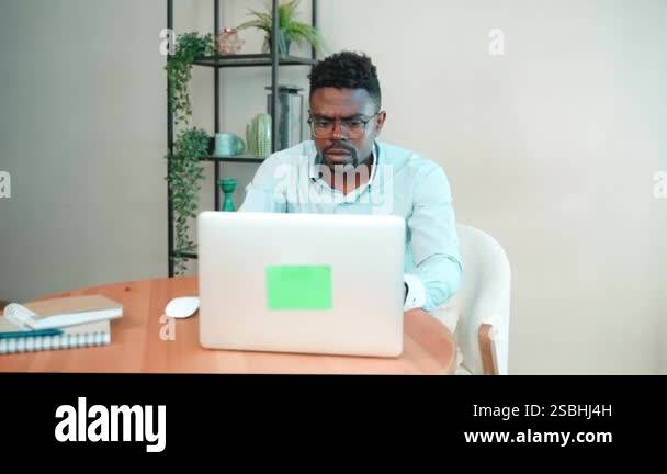 Focused african american man programmer in glasses coding on laptop sitting in workplace in home ...
