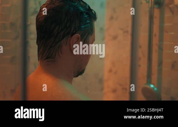 Stressed man taking shower in bathroom. Back view head of guy washing ...