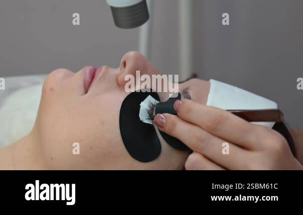 A woman undergoing eyelash extension procedure using an ultraviolet ...