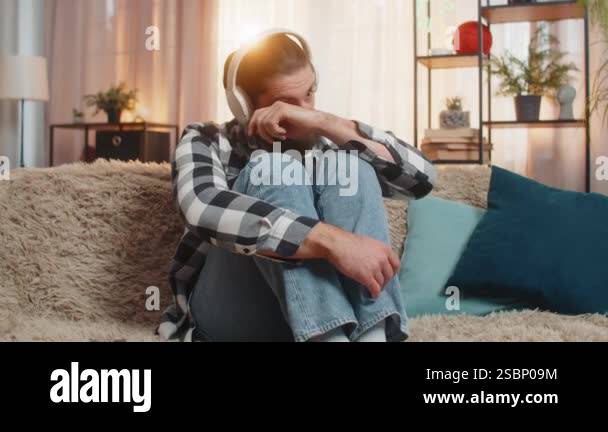 Young man sits at home wearing headphones, listening to emotional tune ...