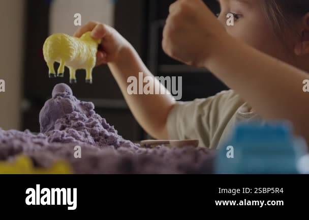 A child engages with purple kinetic sand and a yellow toy duck ...