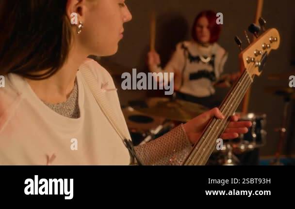 Punk girl energetically playing bass guitar, while her friend with dyed ...