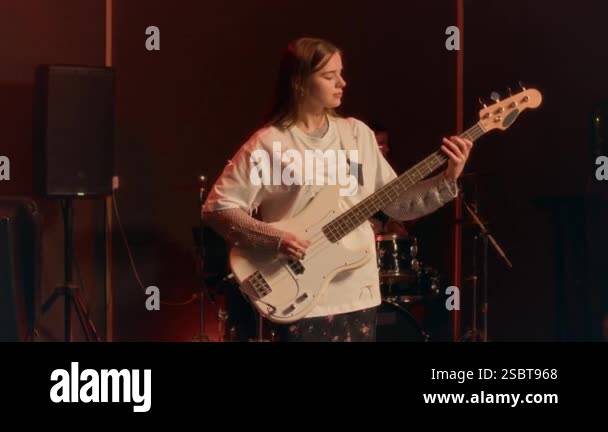 Focused young woman in punk outfit playing white electric bass guitar ...