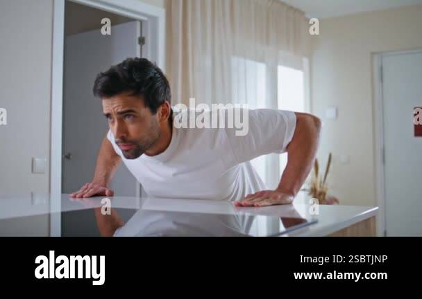 Man making push ups with effort near kitchen countertop at home workout ...