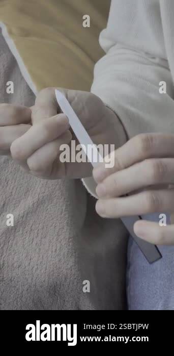 A person carefully filing their nails with a metal file at home ...