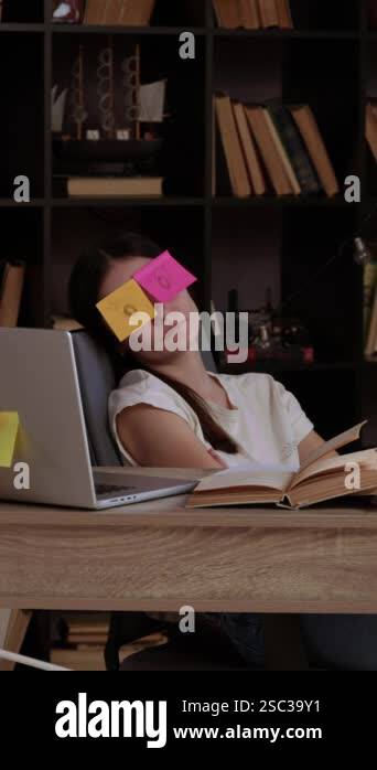 Tired female student at a desk in a beautiful library with her feet up on the table with ...