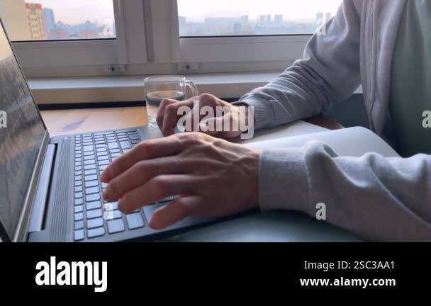 Hands are busy typing on a laptop within a cozy workspace that has a ...