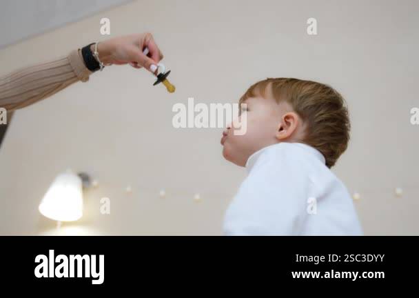 Mom's hand holding and shaking a pacifier above kid's head. Little boy ...
