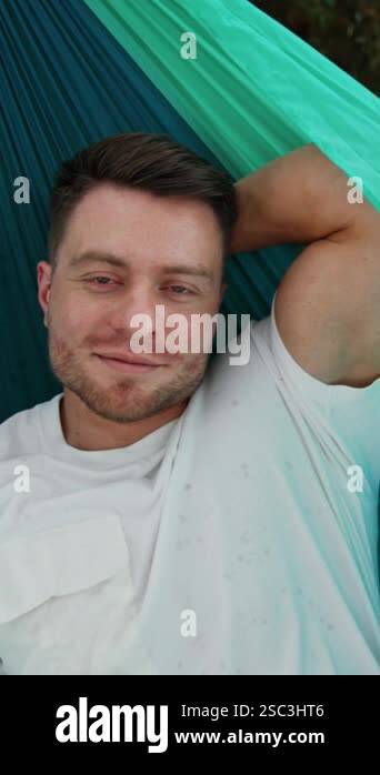 Smiling relaxed Caucasian man lies comfortably in a hammock. Man having ...