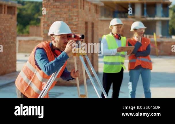 At sunlight man engineer surveyor takes measures with theodolite stand helmet hardhat geodesy ...