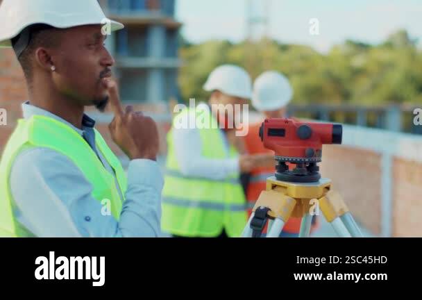 Concentrated African american man engineer surveyor takes measures with theodolite stand helmet ...