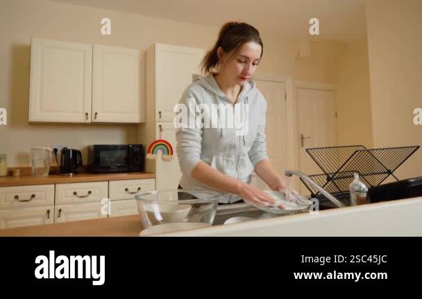 Woman washing dishes at kitchen sink. Female cleaning plates with water ...