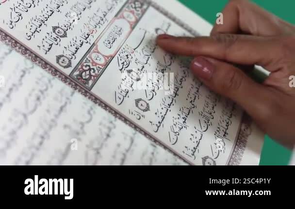 A hand points at an open Quran with Arabic scrip, an Islamic religious ...