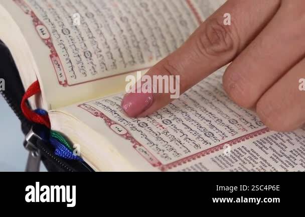A finger points to Arabic script on the open pages of a Quran, a holy ...