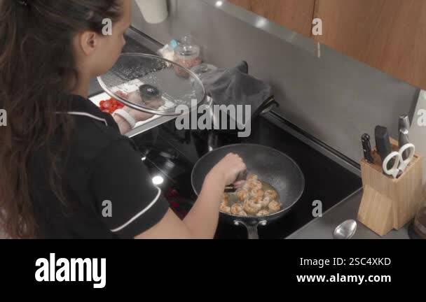 The process of cooking shrimp at home. A woman holds a glass lid in one ...