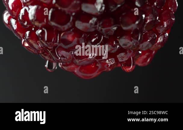 Red pomegranate juice dripping from half of fruit on black background ...