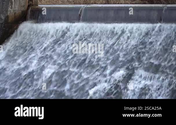 A vigorous water stream cascades over a dam, creating a turbulence ...