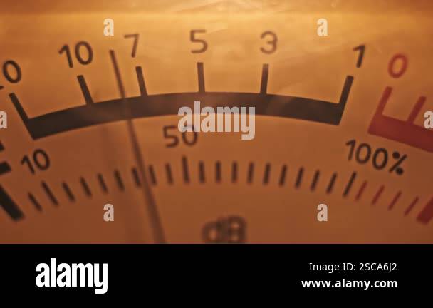 A macro shot of a vintage VU meter with a glowing decibel scale. The ...