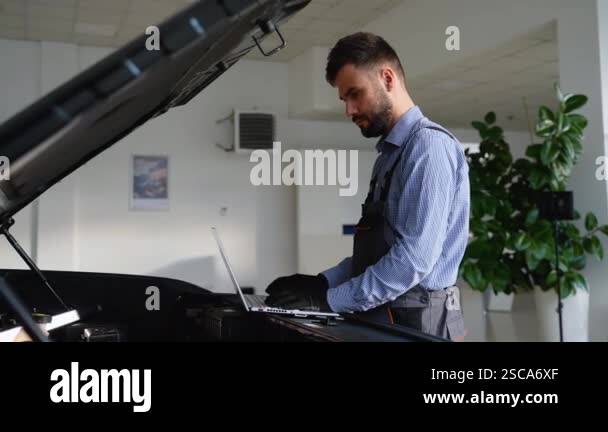 A professional auto mechanic in a modern workshop uses a laptop to ...