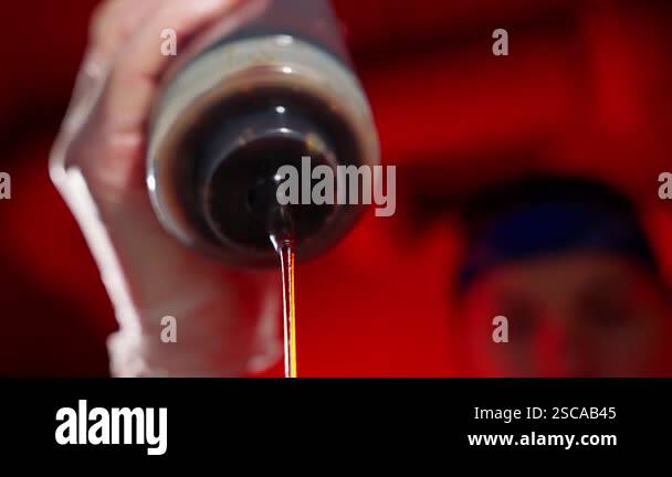 A gloved hand pours dark sauce from a bottle with precision against a ...