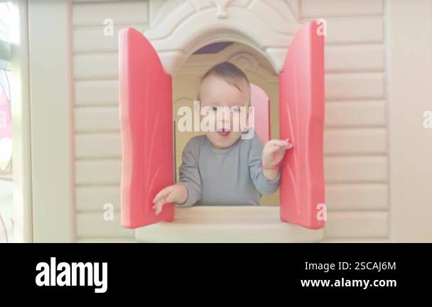 Happy baby boy playing hide and seek, opening and closing the window ...
