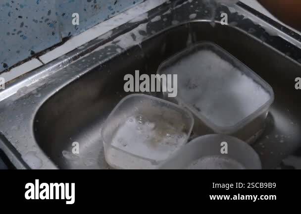A man rinsing dishes to remove soap foam in the kitchen sink. The water ...